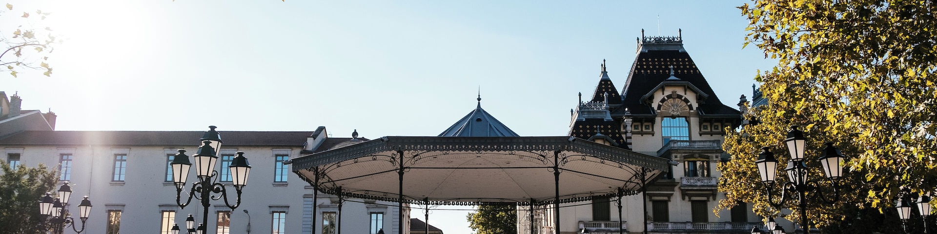 Uma praça de paralelepípedos com um coreto, edifícios históricos e árvores.