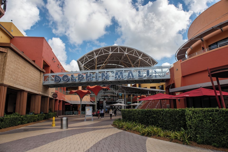 Entrada do Dolphin Mall, com um arco grande e guarda-sóis vermelhos.
