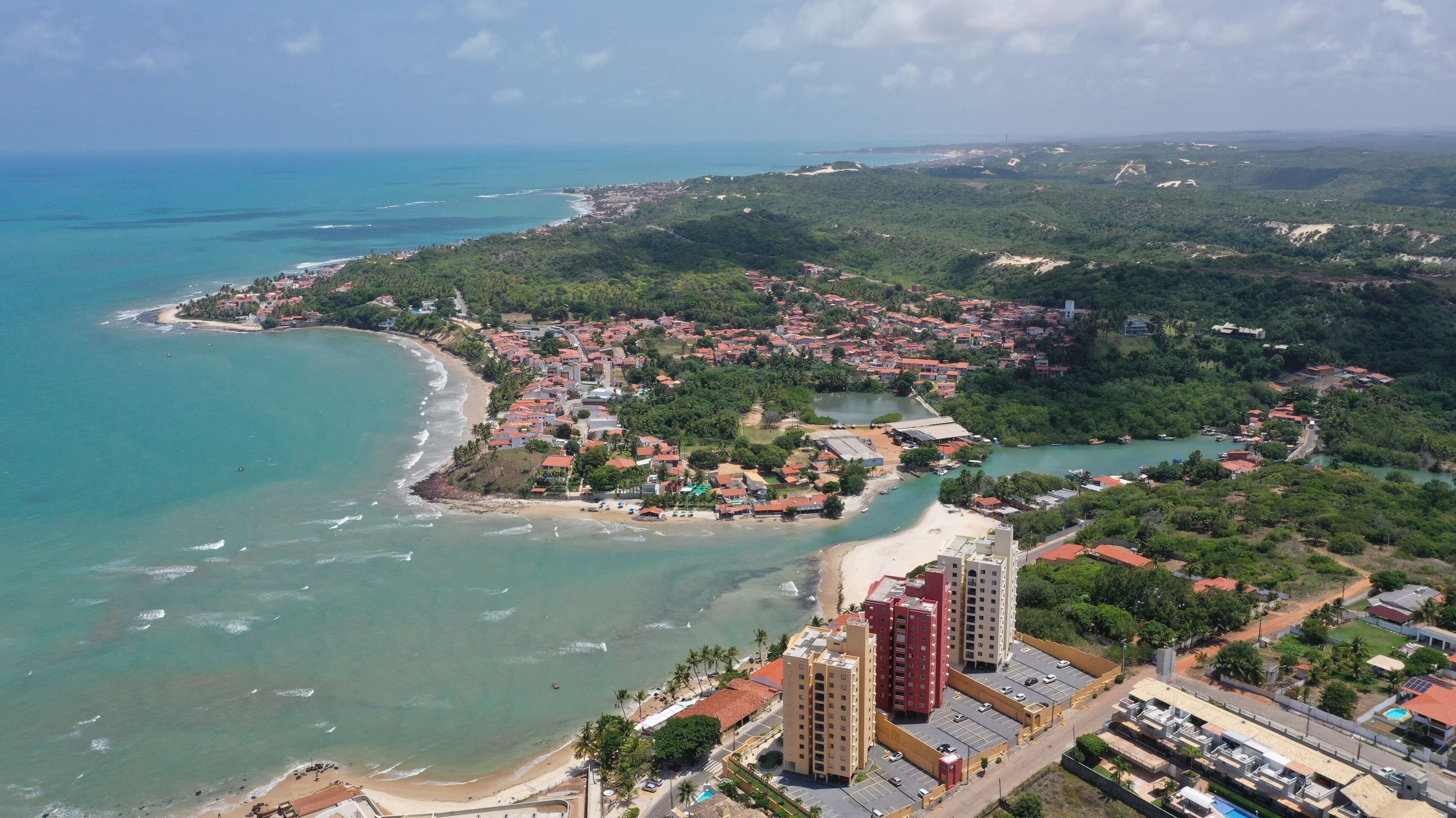 Uma vila costeira com praia, rio e montanhas ao fundo.