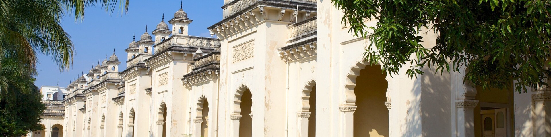 Uma fileira de edifícios ornamentados com torres em cúpula e arcos, cercada por jardins bem cuidados e caminhos.