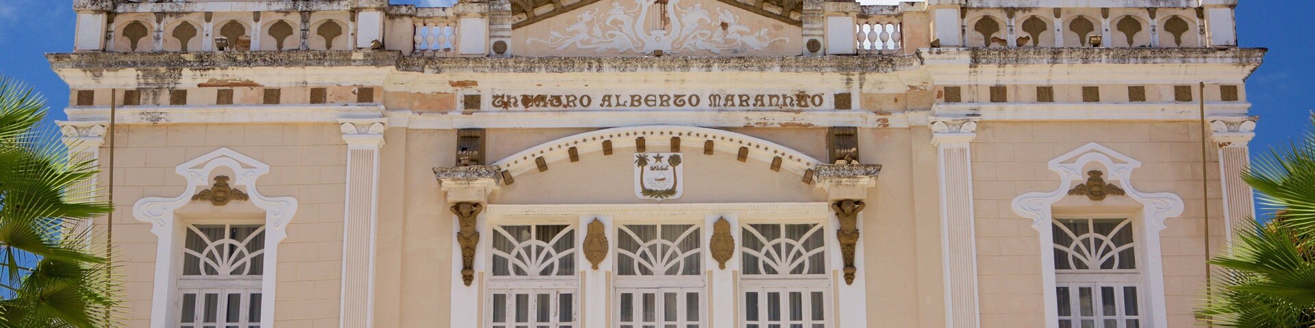 Um edifício histórico com varandas ornamentadas, uma estátua central e um brasão acima da entrada.