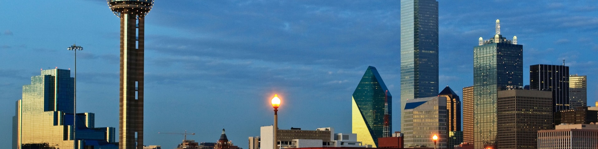 Horizonte urbano com arranha-céus modernos, uma torre imponente e uma autoestrada com rastros de luz.