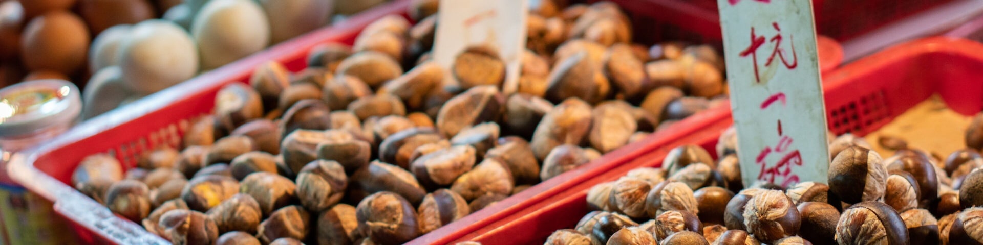 Uma banca de mercado com diversos tipos de frutos secos, incluindo avelãs e nozes, expostos em cestos vermelhos.