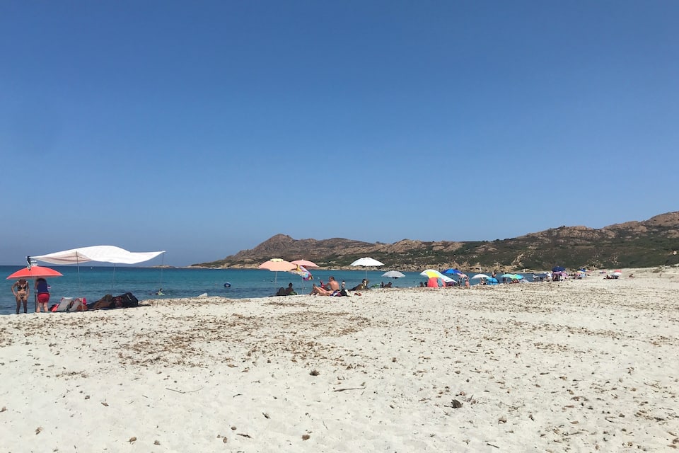Uma praia com pessoas, guarda-sóis e montanhas ao fundo.