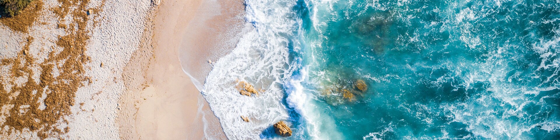 Uma praia com ondas quebrando em formações rochosas.