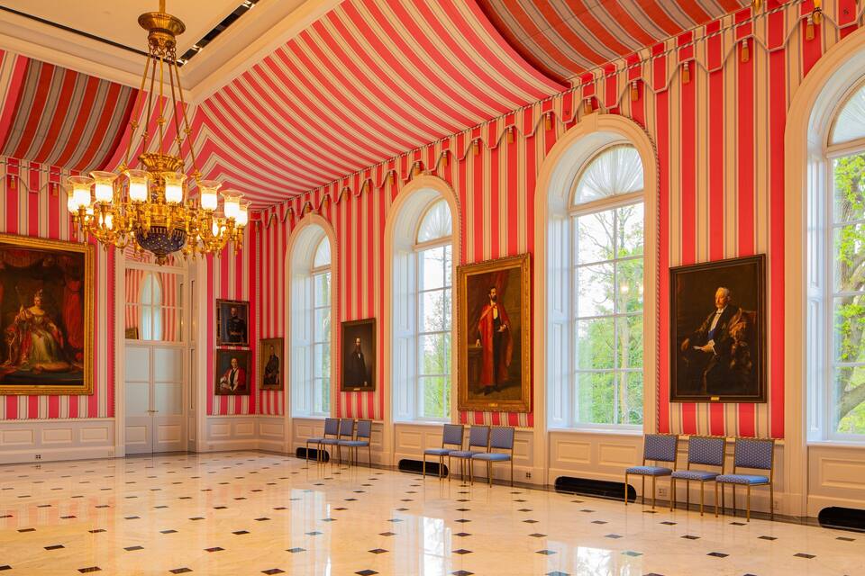 Um quarto com paredes listradas em vermelho e branco, grandes janelas arqueadas e um lustre.