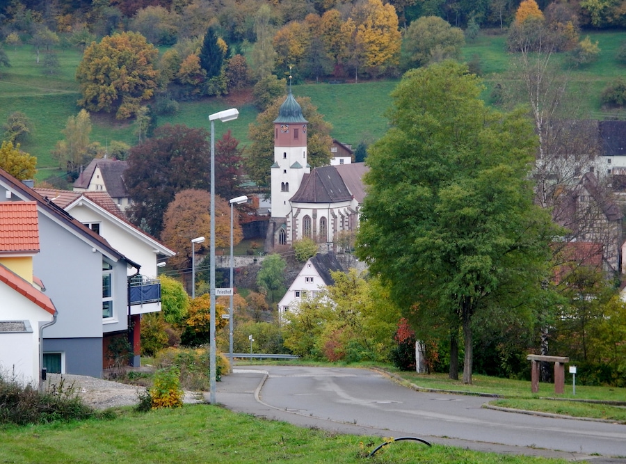 Uma cidade com uma igreja, casas e uma colina ao fundo.