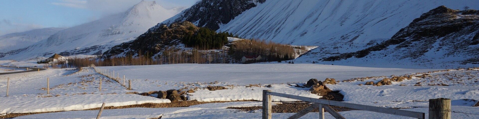 Paisagem coberta de neve com um portão de madeira, montanhas e céu claro.