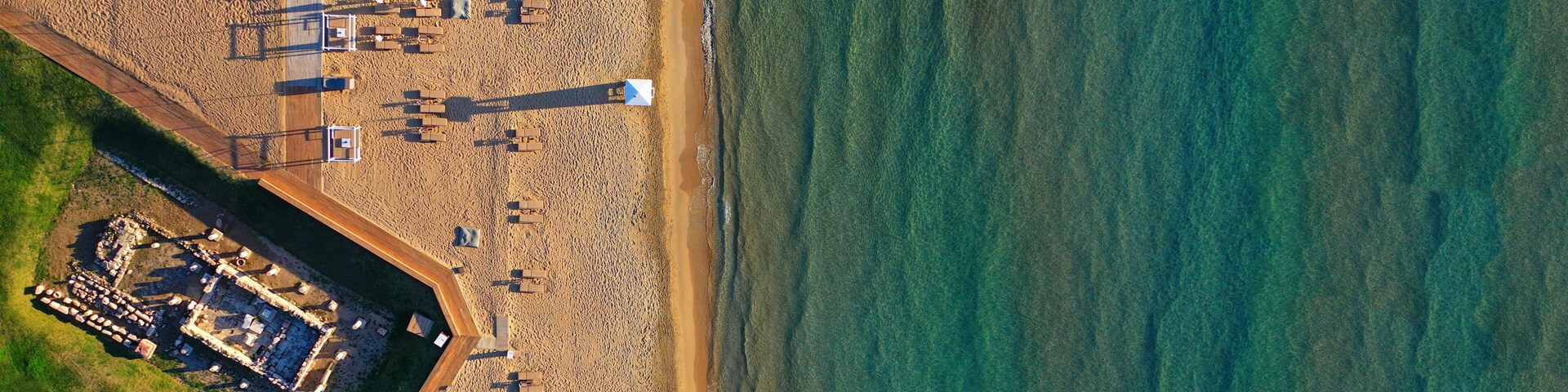 Vista aérea de uma área costeira com uma praia de areia, um píer e uma área cercada com construções.