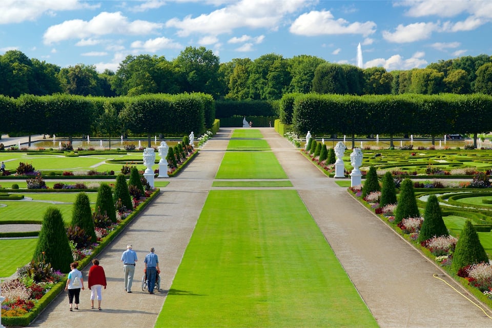 Um jardim formal com um caminho central, gramados bem cuidados e estátuas.