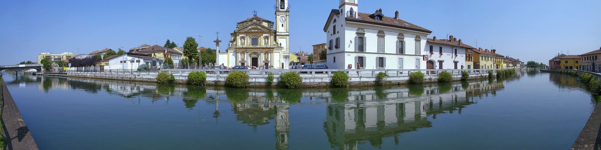 Um canal com edifícios refletidos na água, uma torre do relógio e uma ponte.