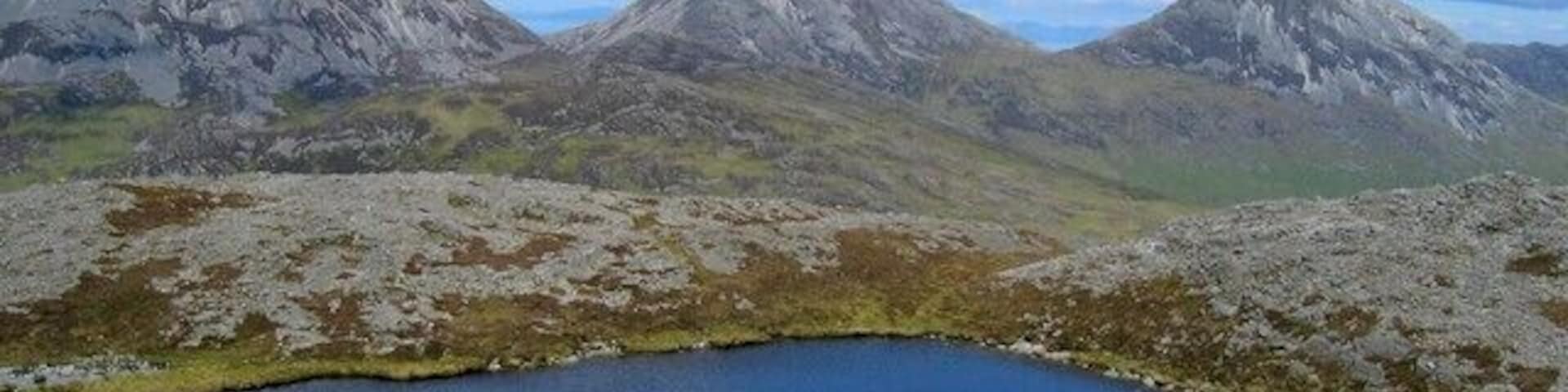 Paisagem montanhosa com um pequeno lago rodeado por terreno rochoso.