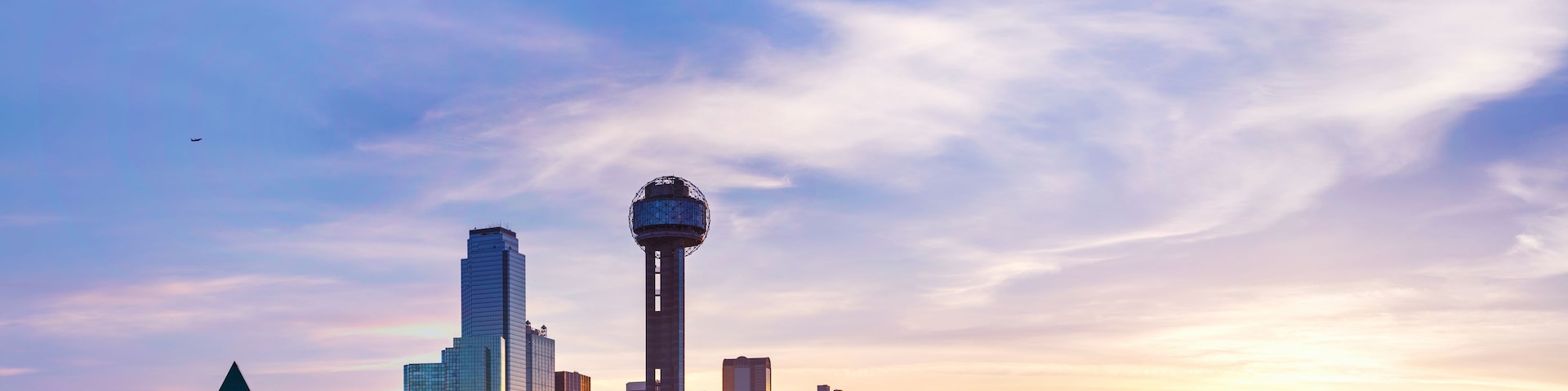 Horizonte urbano com uma torre imponente e arranha-céus sob um céu ao pôr do sol.