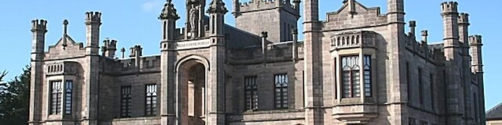 Um grande edifício histórico de pedra, com várias torres e janelas em arco.