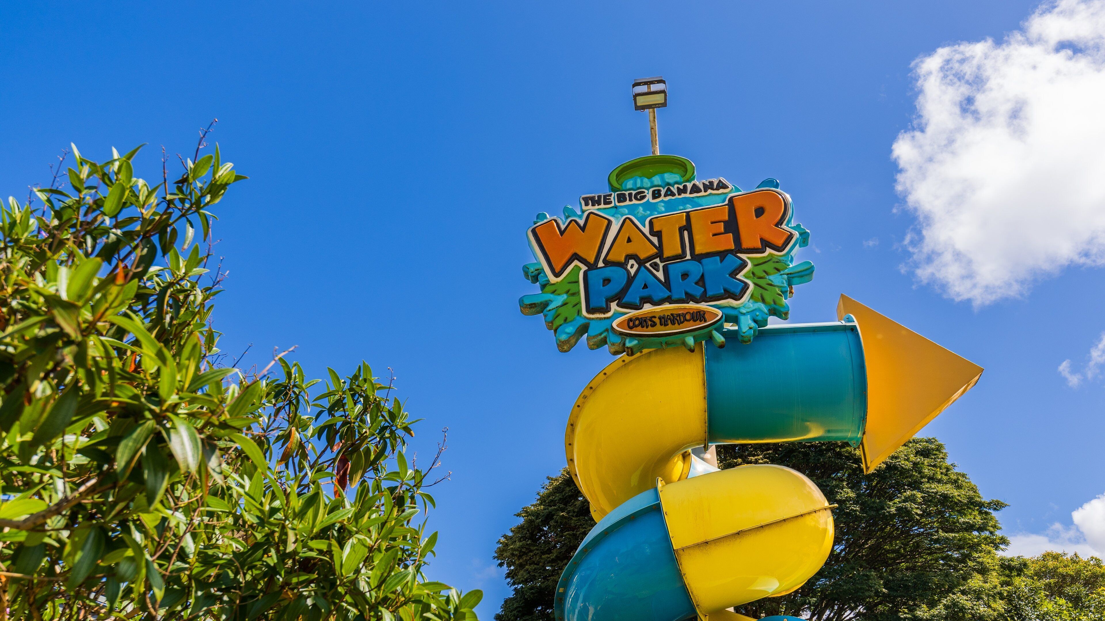 Um letreiro colorido para o Parque Aquático Big Banana, com um grande escorregador aquático amarelo e azul.