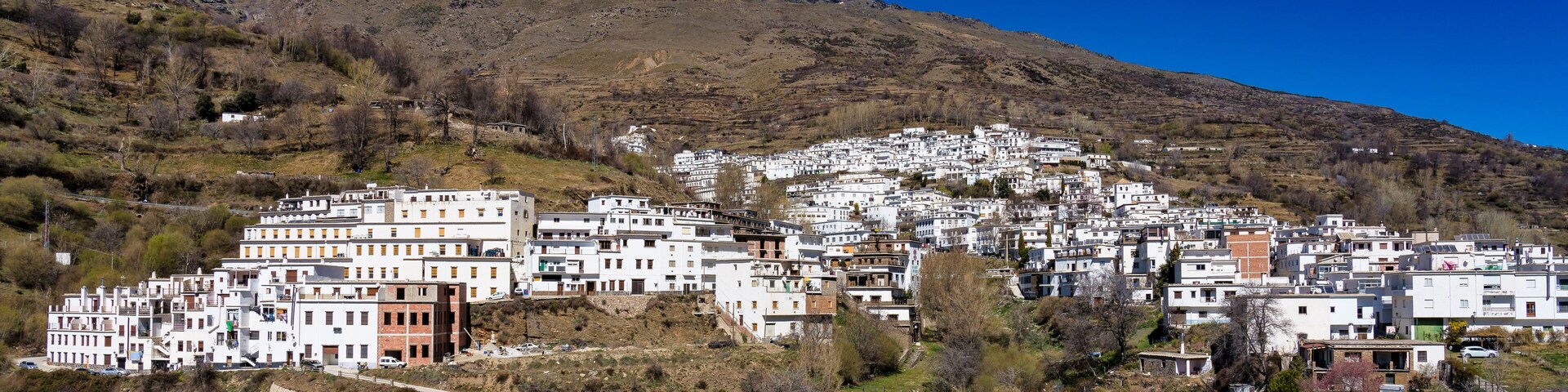 Uma povoação na encosta com edifícios brancos e montanhas ao fundo.