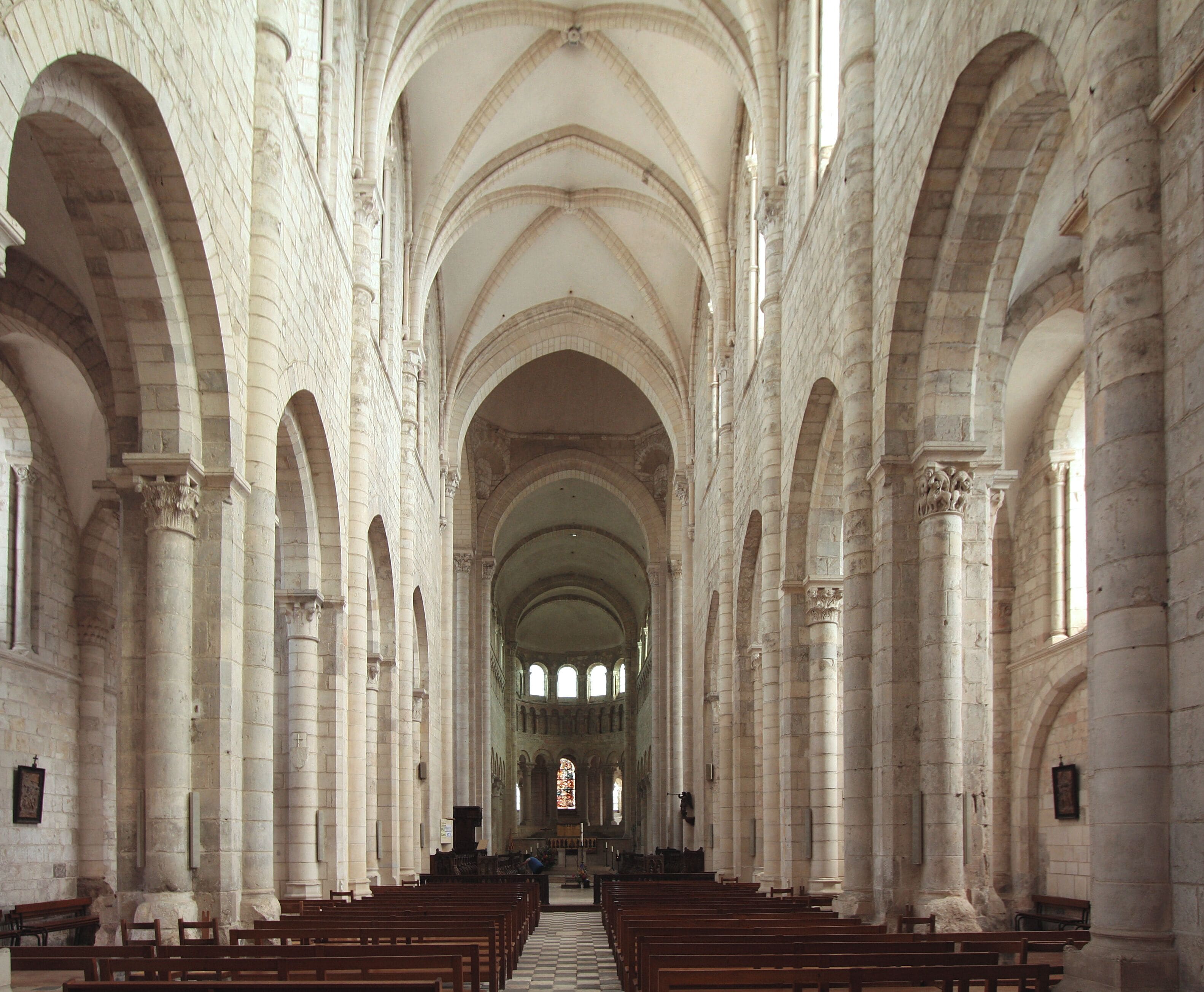 Interior de uma catedral com tetos abobadados altos, colunas em arco e fileiras de bancos.