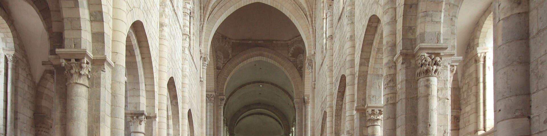 Interior de uma catedral com tetos abobadados altos, colunas em arco e fileiras de bancos.