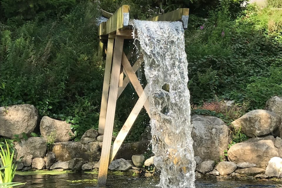 Uma cascata sobre rochas alimenta um lago cercado por vegetação.