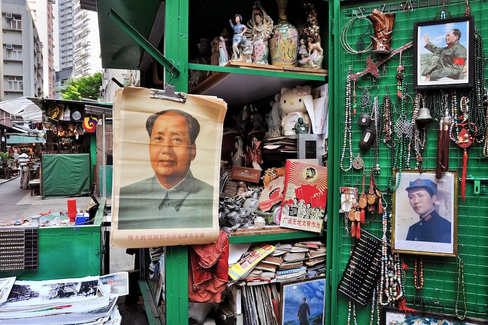 Loja desorganizada com diversos objetos, incluindo um grande retrato, figuras e uma placa verde.