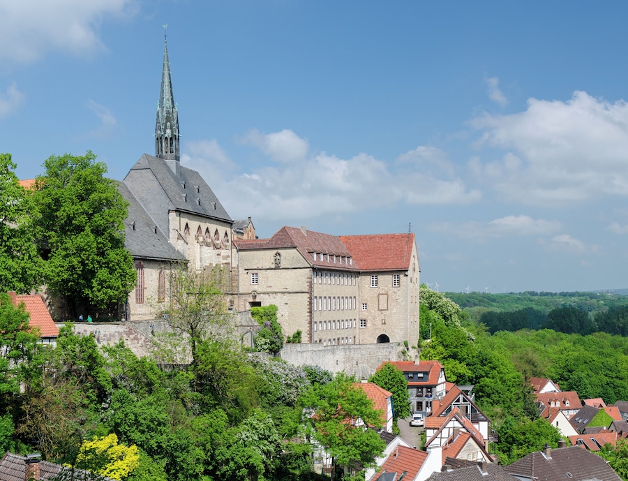 Um castelo histórico com uma torre alta, rodeado por vegetação exuberante e casas tradicionais.