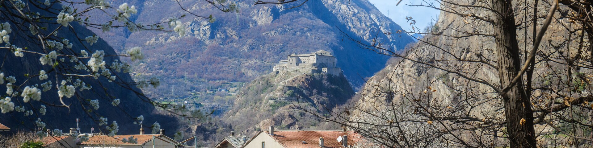 Paisagem montanhosa com uma aldeia, vinhedos e um castelo imponente.