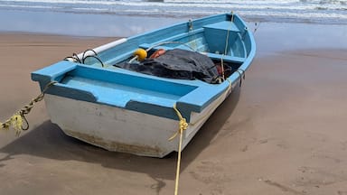Um pequeno barco azul amarrado a uma praia de areia, com o oceano ao fundo.