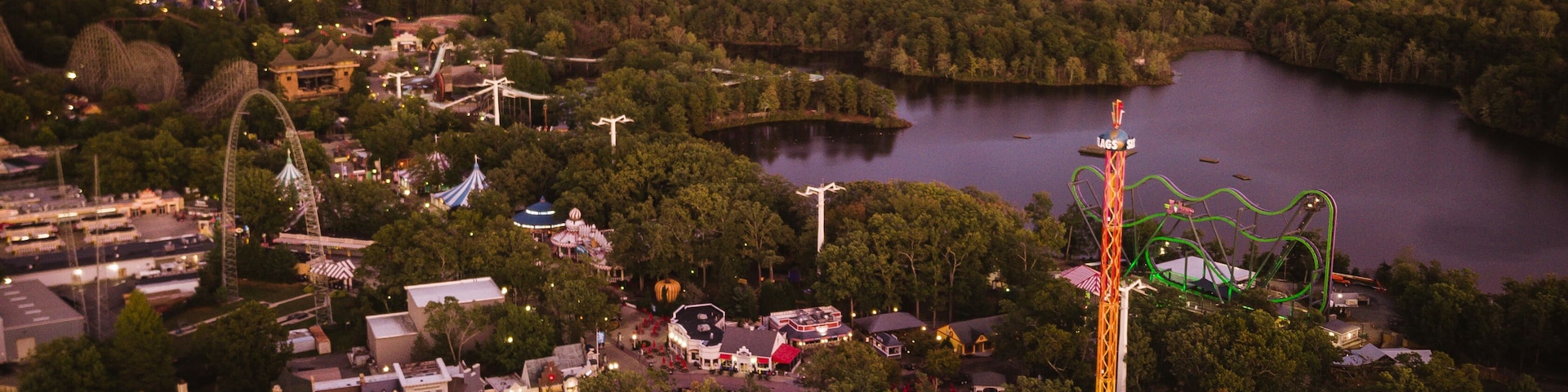 Um parque temático com roda gigante, montanha-russa e uma torre alta.