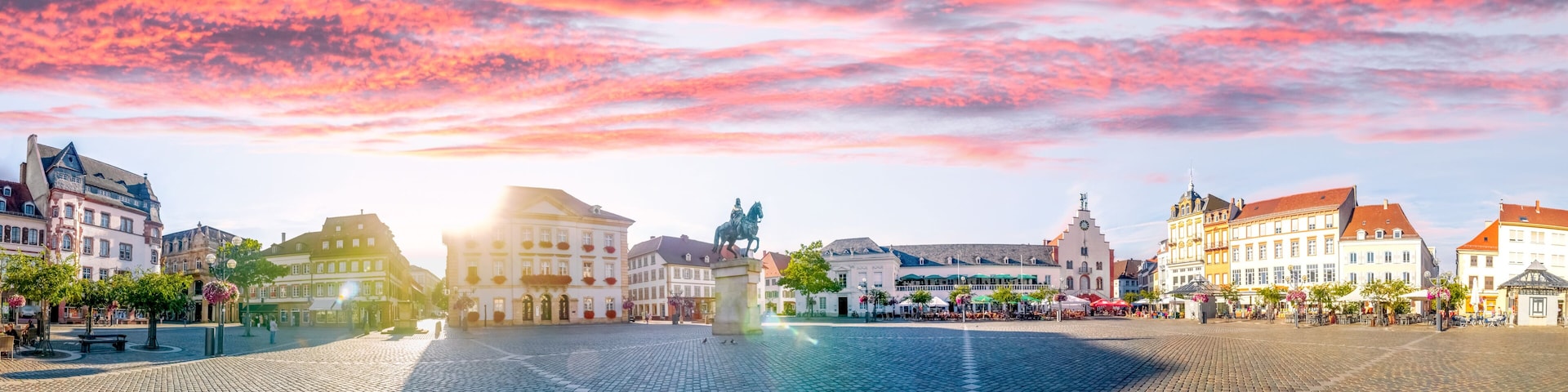 Uma praça de paralelepípedos com edifícios históricos, uma estátua e uma igreja.