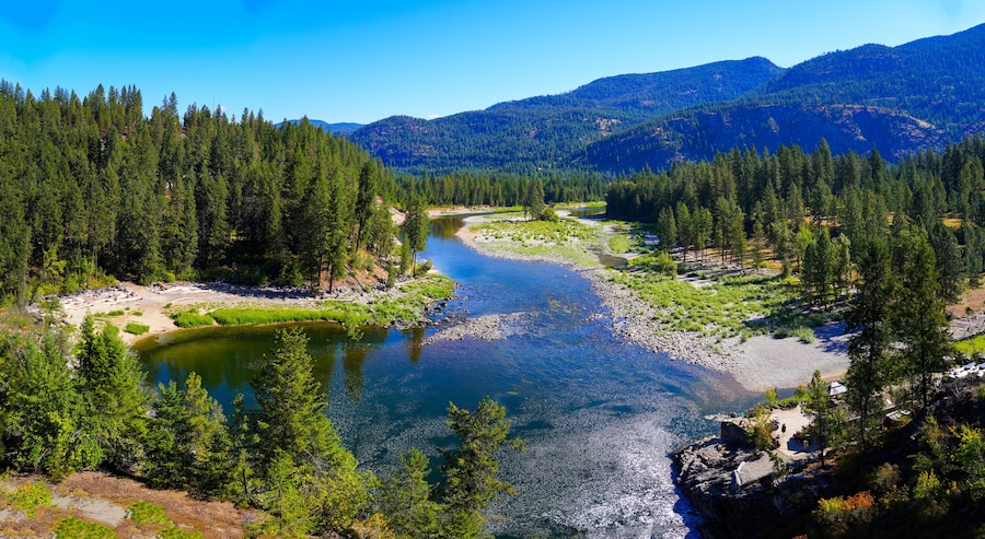 Um rio serpenteia por um vale arborizado, com montanhas ao fundo.
