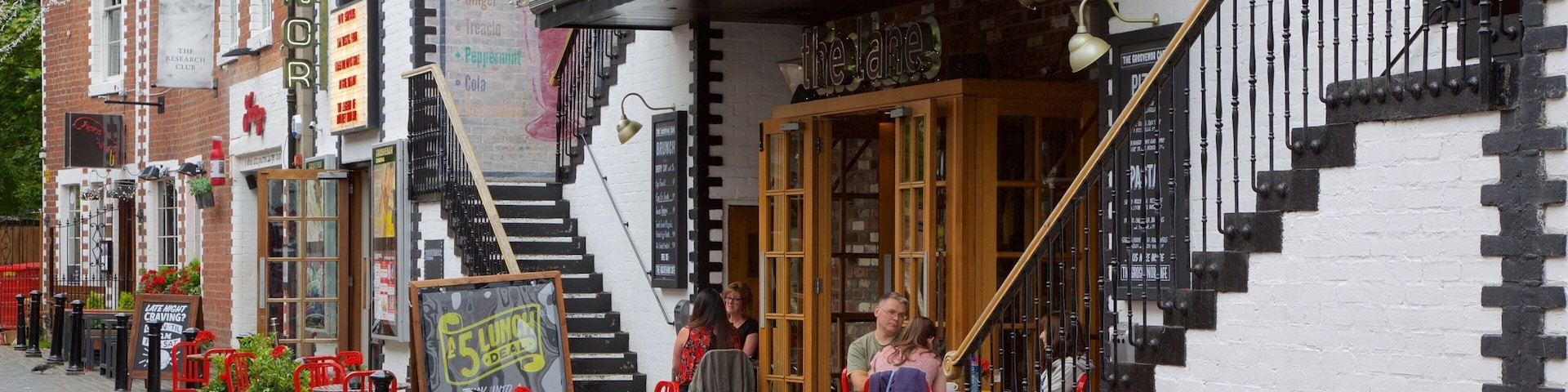 Rua com cadeiras e mesas vermelhas em frente a um café.