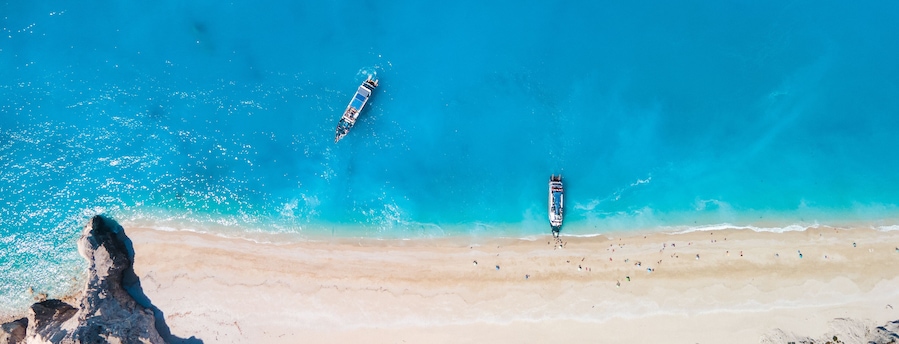 Uma praia com águas turquesa cristalinas, dois barcos e um afloramento rochoso.