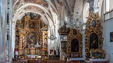 Interior de igreja ornamentado, com altos tetos, afrescos detalhados e um altar central.