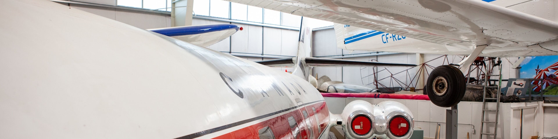 Um avião branco e vermelho com listras azuis, uma hélice e um leme vermelho, dentro de um hangar.