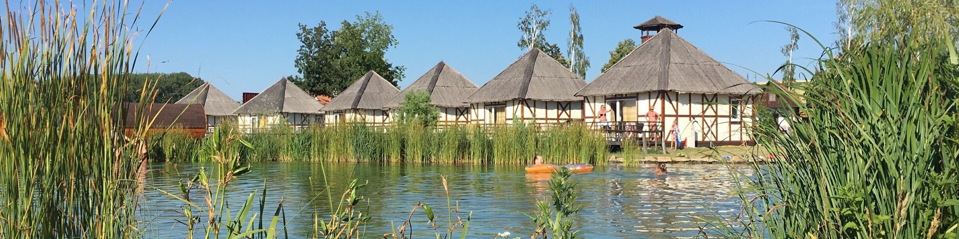 Um lago calmo com cabanas de telhado de palha e vegetação exuberante.