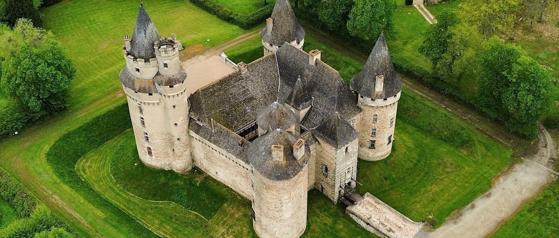 Vista aérea de um castelo rodeado por vegetação exuberante e uma pequena aldeia.