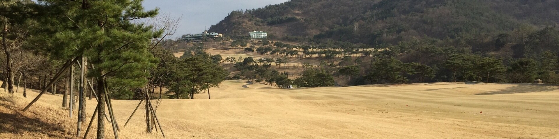 Um campo de golfe com uma montanha ao fundo e um edifício na encosta.