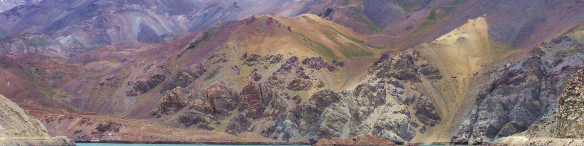 Paisagem montanhosa com um lago azul-turquesa rodeado por terreno acidentado.