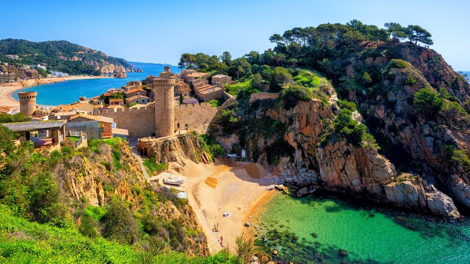 Uma vila costeira com um castelo histórico, uma praia e um penhasco rochoso.