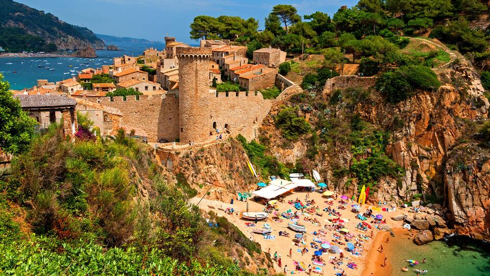 Uma cidade costeira com um castelo histórico, uma praia arenosa e uma vista desobstruída do mar.