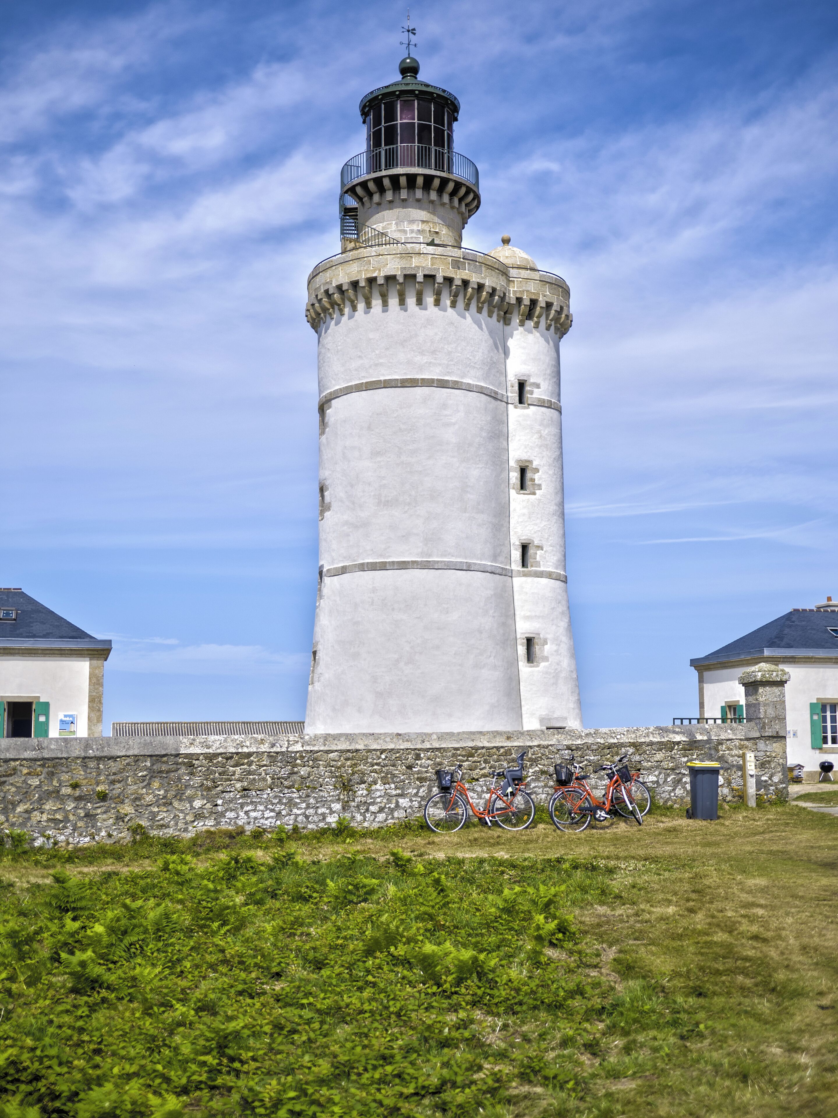 Um farol com base de pedra e torre cilíndrica, coroada por uma girândola.