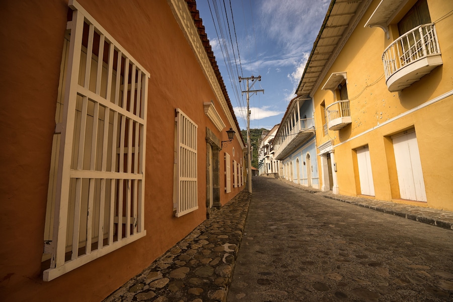Ruas de paralelepípedos ladeadas por edifícios com venezianas brancas e varandas.