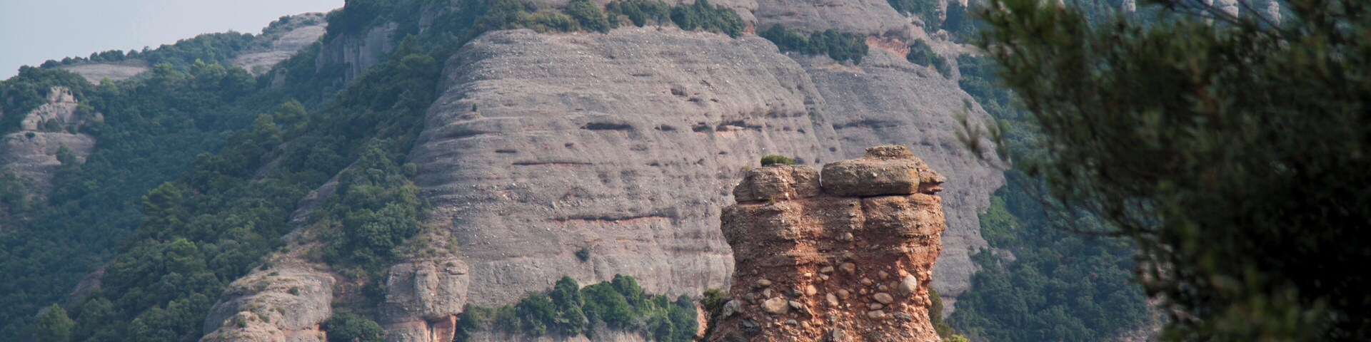 Montanha acidentada com formação rochosa imponente e vegetação verde densa.