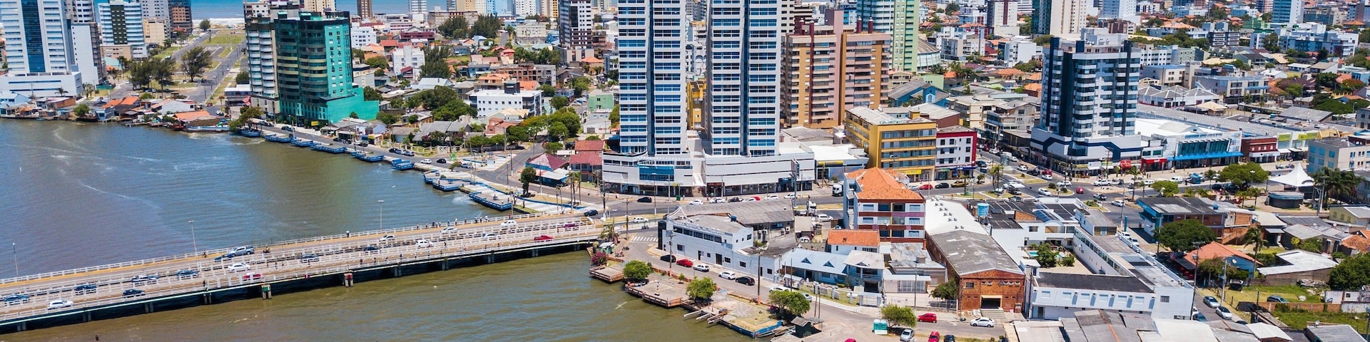 Paisagem costeira urbana com uma ponte imponente, edifícios urbanos densos e vista clara do mar.