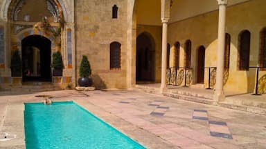 Um pátio com piscina, arcos e piso de azulejos.