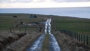 Um caminho costeiro com cabanas, uma cerca e uma paisagem gramada.