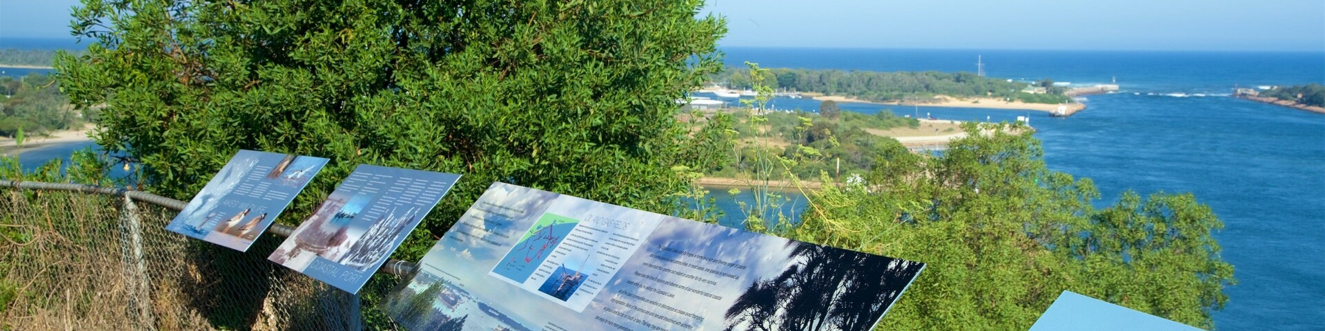 Ponto de vista costeiro com painéis informativos e vista do mar.