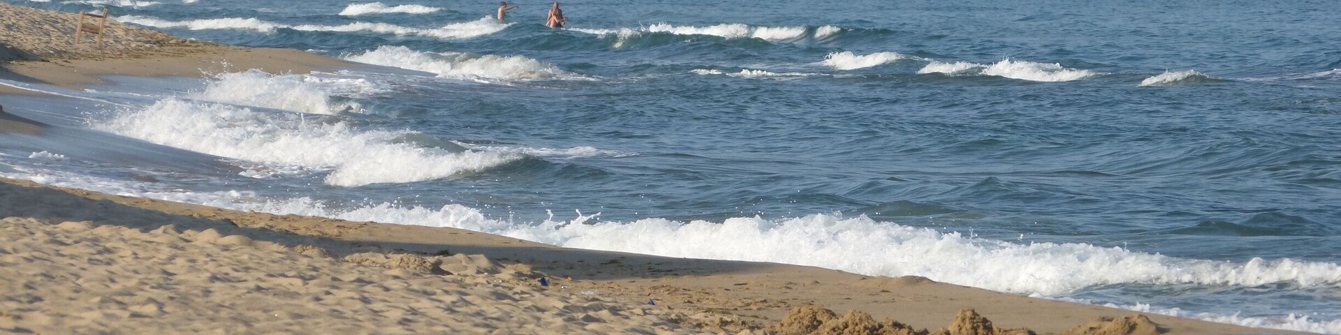 Uma praia arenosa com ondas quebrando na costa e falésias ao fundo.