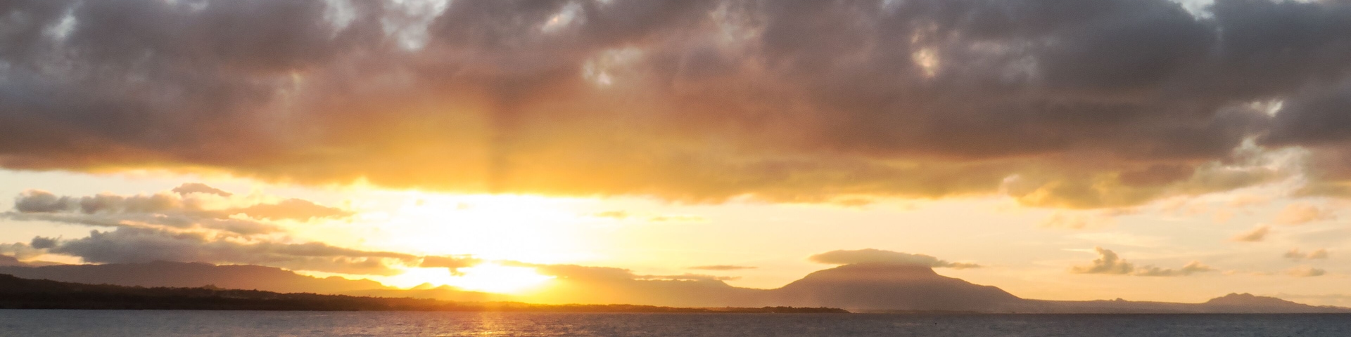 Um pôr do sol sobre a água, com nuvens e paisagens distantes.