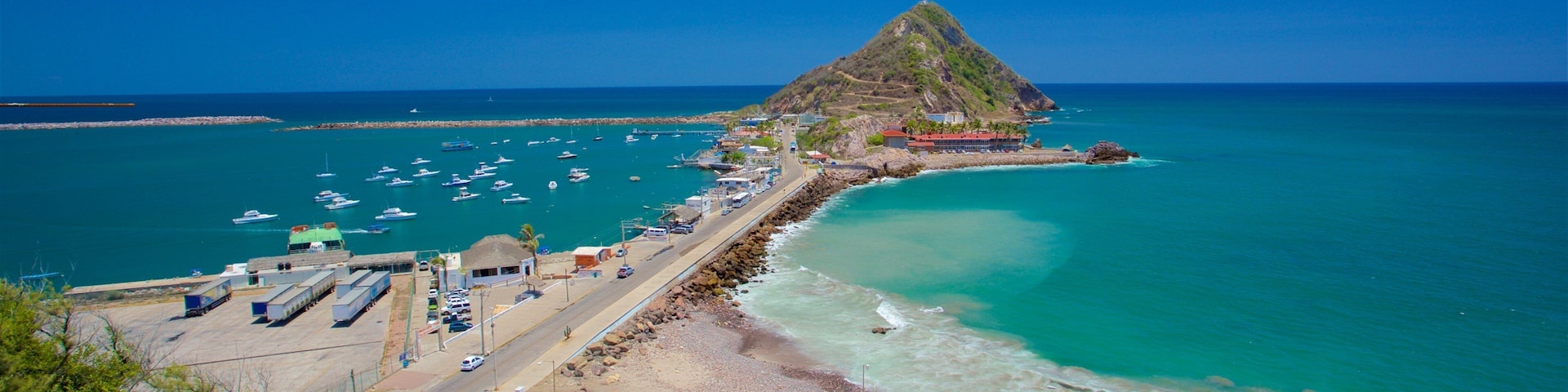 Uma cidade costeira com uma montanha imponente, uma marina com barcos e uma estrada pavimentada que leva à praia.